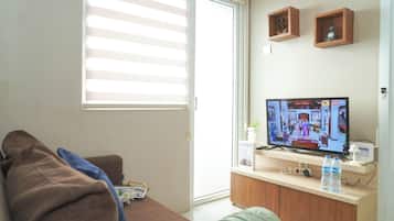 Uma sala de estar com sofá, televisão, armário de madeira e janela com persianas.