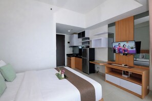 Quarto de hotel com cama, televisão, cozinha compacta e área de estar.