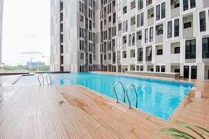 Um edifício moderno com piscina, várias varandas e vista para guindastes de construção ao fundo.