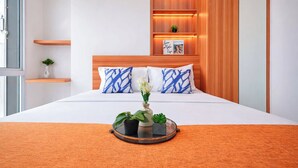 Quarto de hotel moderno com uma cama grande, cabeceira de madeira, uma prateleira pequena com uma planta e um quadro na parede.