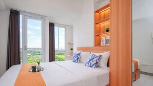 Quarto de hotel moderno com uma cama grande, cabeceira de madeira, uma prateleira pequena com objetos decorativos e vista da cidade através de grandes janelas.