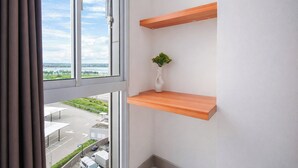Canto de um quarto com uma janela, um vaso branco com plantas verdes e duas prateleiras de madeira.