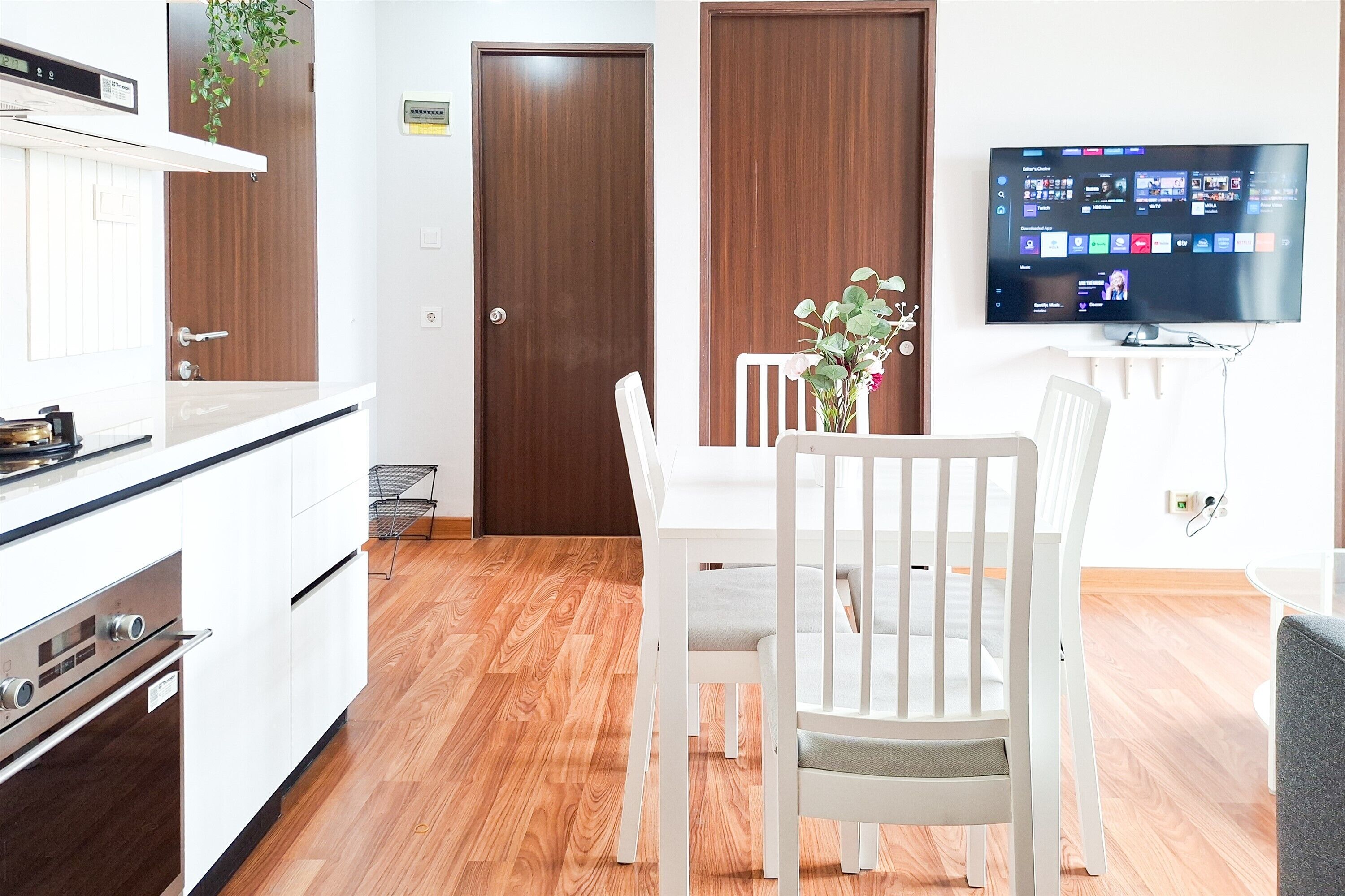 Cozinha moderna com armários brancos, forno embutido e área de refeições com mesa e cadeiras brancas.