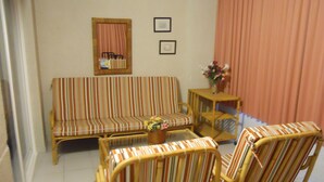 Uma sala de estar com um sofá listrado, duas poltronas, uma mesinha e um espelho na parede.