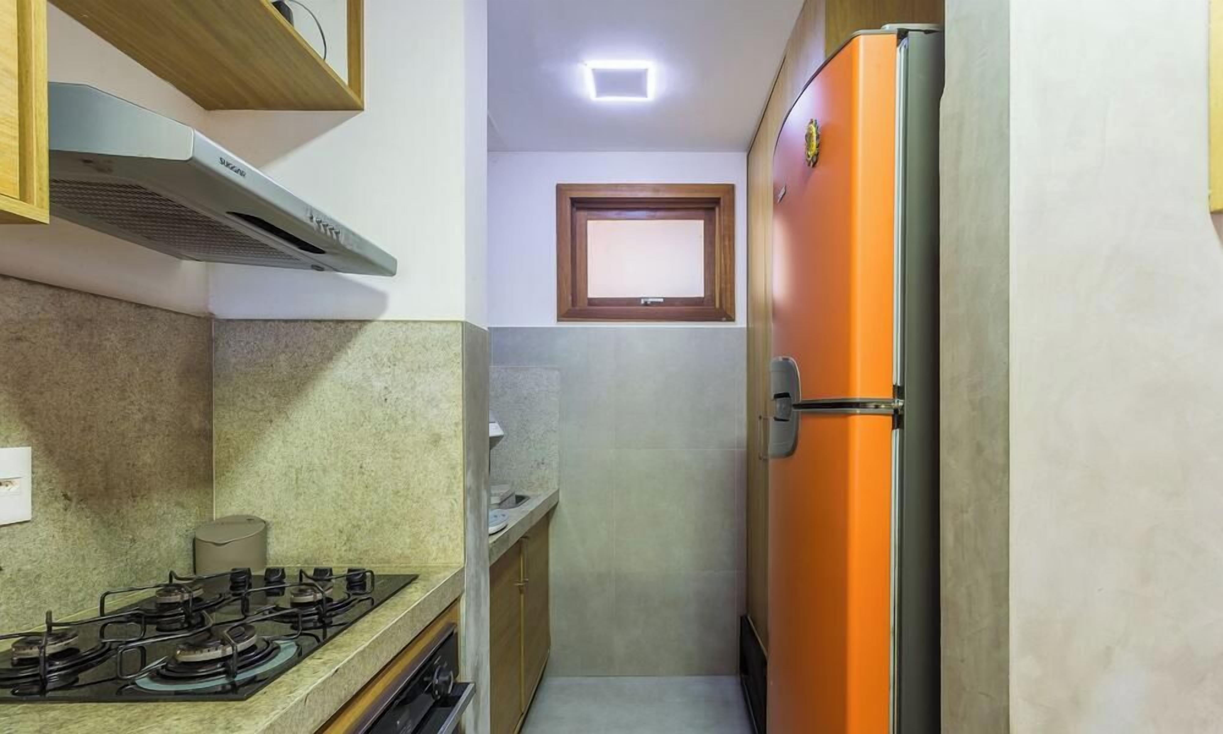 Cozinha compacta com fogão a gás, forno embutido, coifa de aço inoxidável e uma pequena janela.
