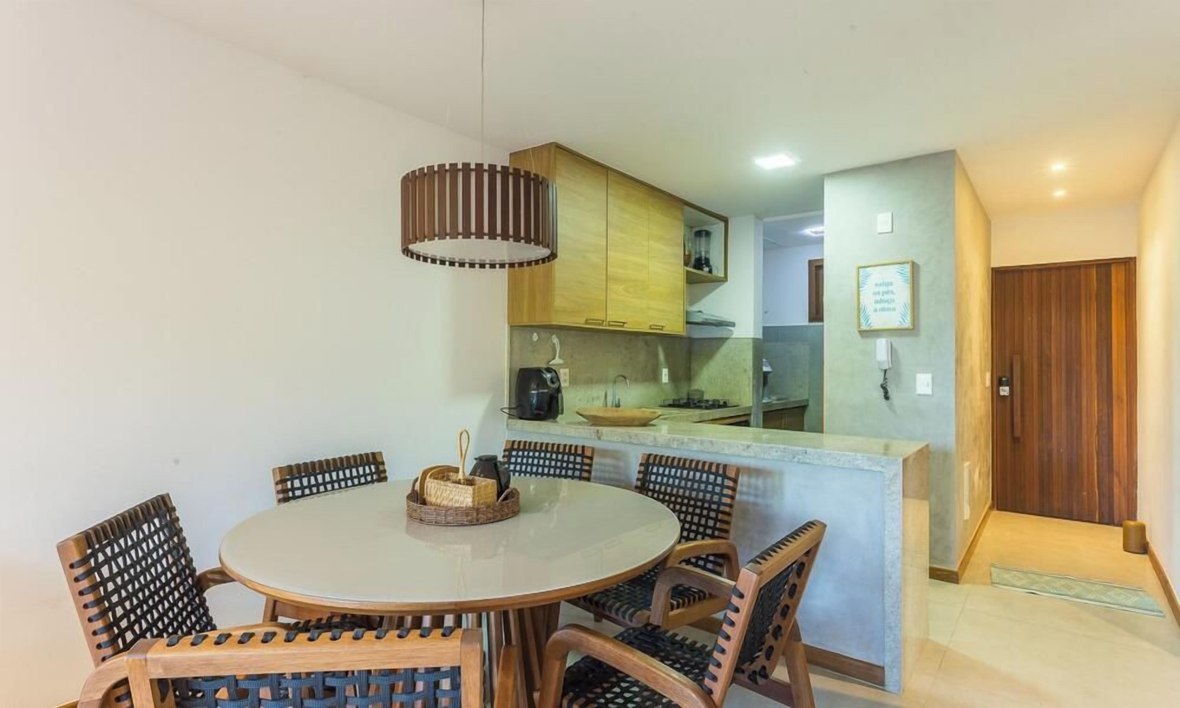 Uma sala de jantar com mesa redonda e cadeiras, uma cozinha com armários de madeira e um lustre.
