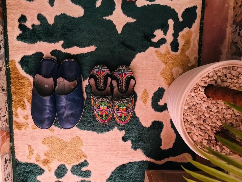 Um par de sapatos sobre um tapete estampado, uma tigela com pedrinhas e uma planta.