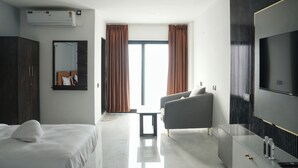 Quarto de hotel moderno com cama, sofá, televisão e uma janela grande com cortinas.