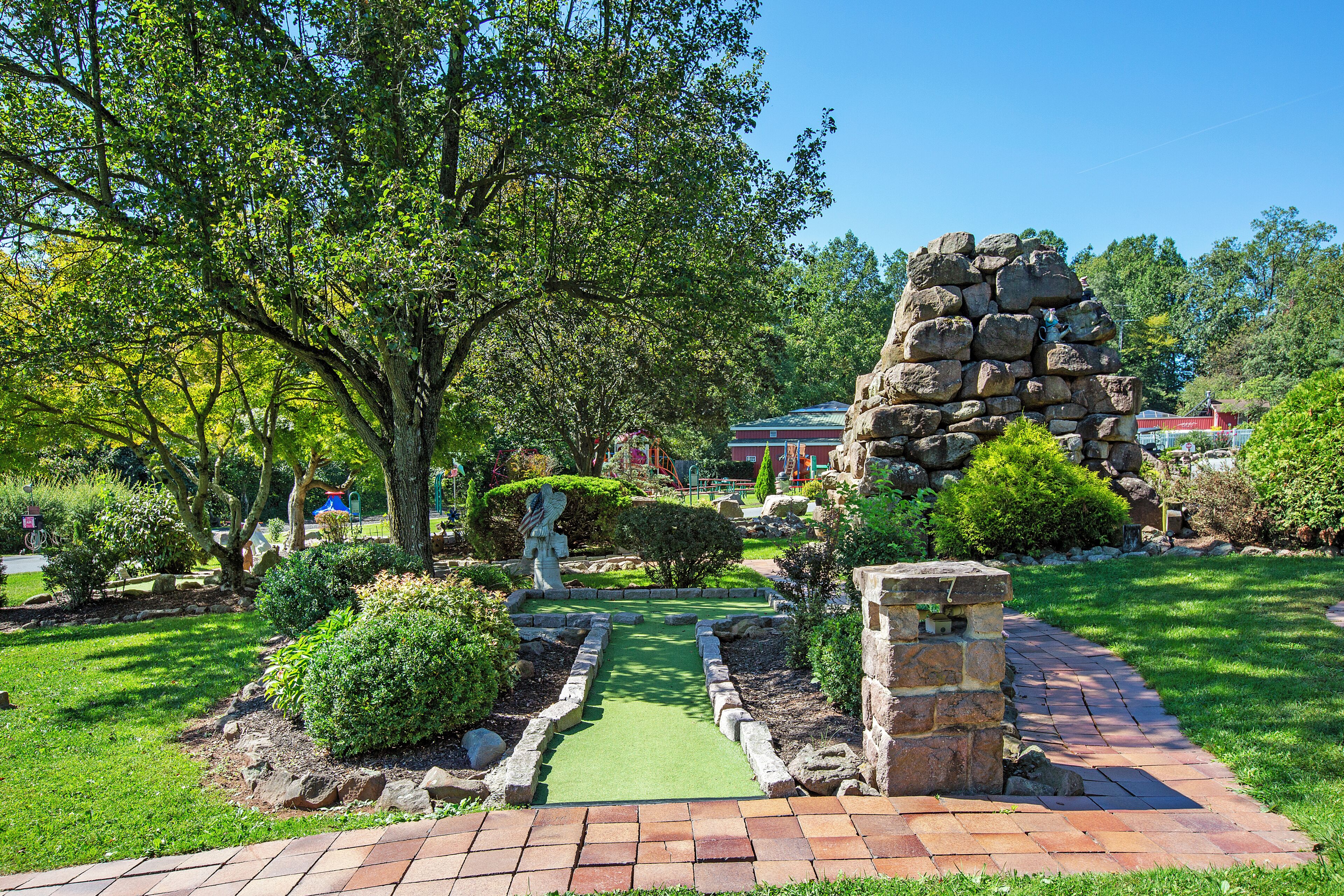 Um jardim com um campo de mini golfe, estruturas de pedra e diversas árvores e arbustos.