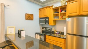 Uma cozinha moderna com armários de madeira, geladeira de aço inoxidável, micro-ondas e fogão. Há banquetas e um certificado emoldurado no balcão.