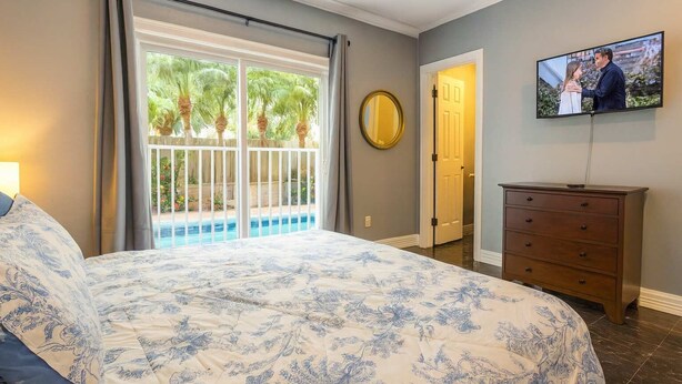 Quarto com cama, televisão, cômoda e porta de vidro corrediça para uma varanda.
