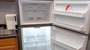Geladeira aberta com várias prateleiras e gavetas, máquina de gelo embutida e dispenser de água.