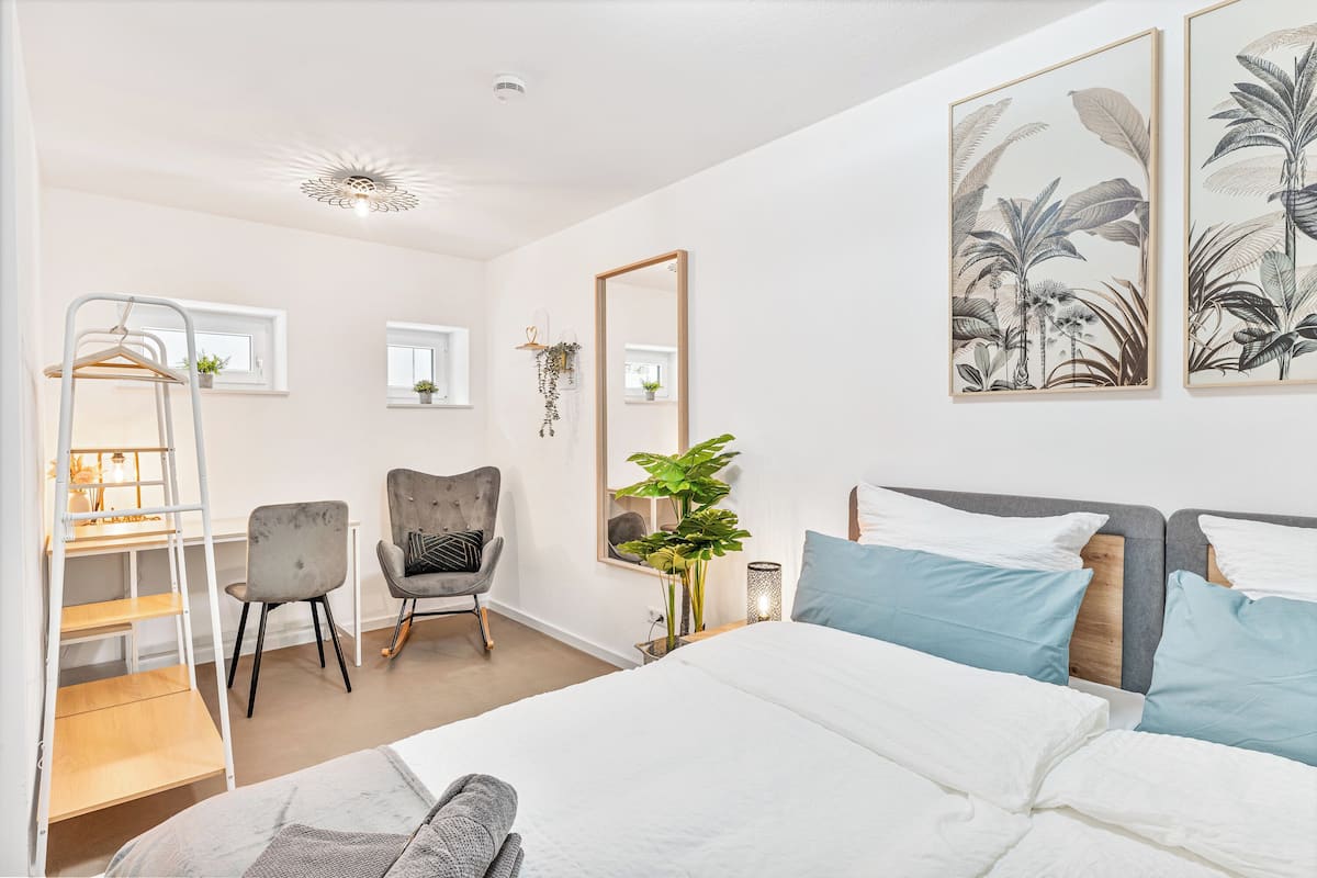 Quarto moderno com cama, duas cadeiras, escrivaninha e espelho.