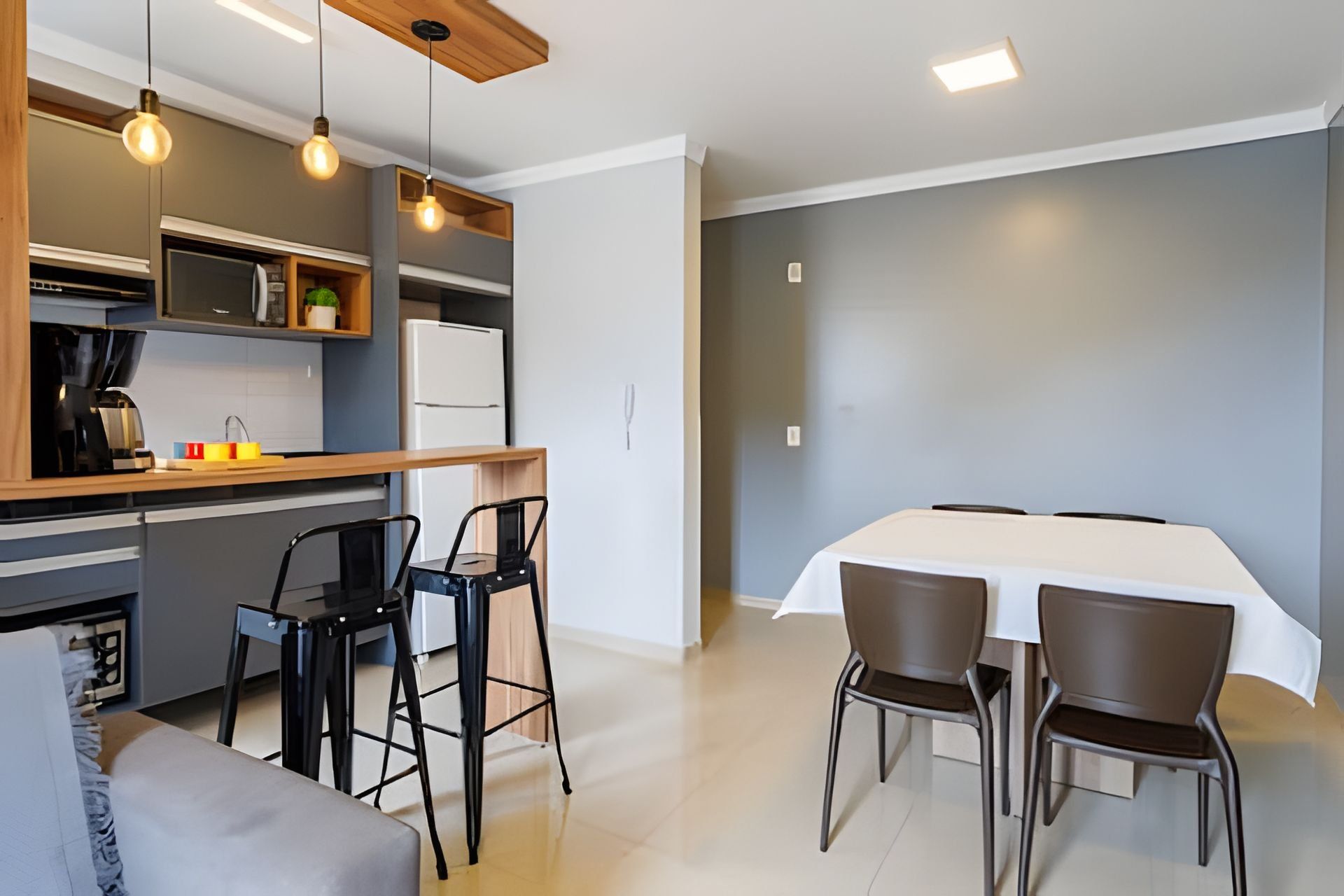 Cozinha moderna com área de refeições, incluindo uma mesa e cadeiras, e uma geladeira embutida.