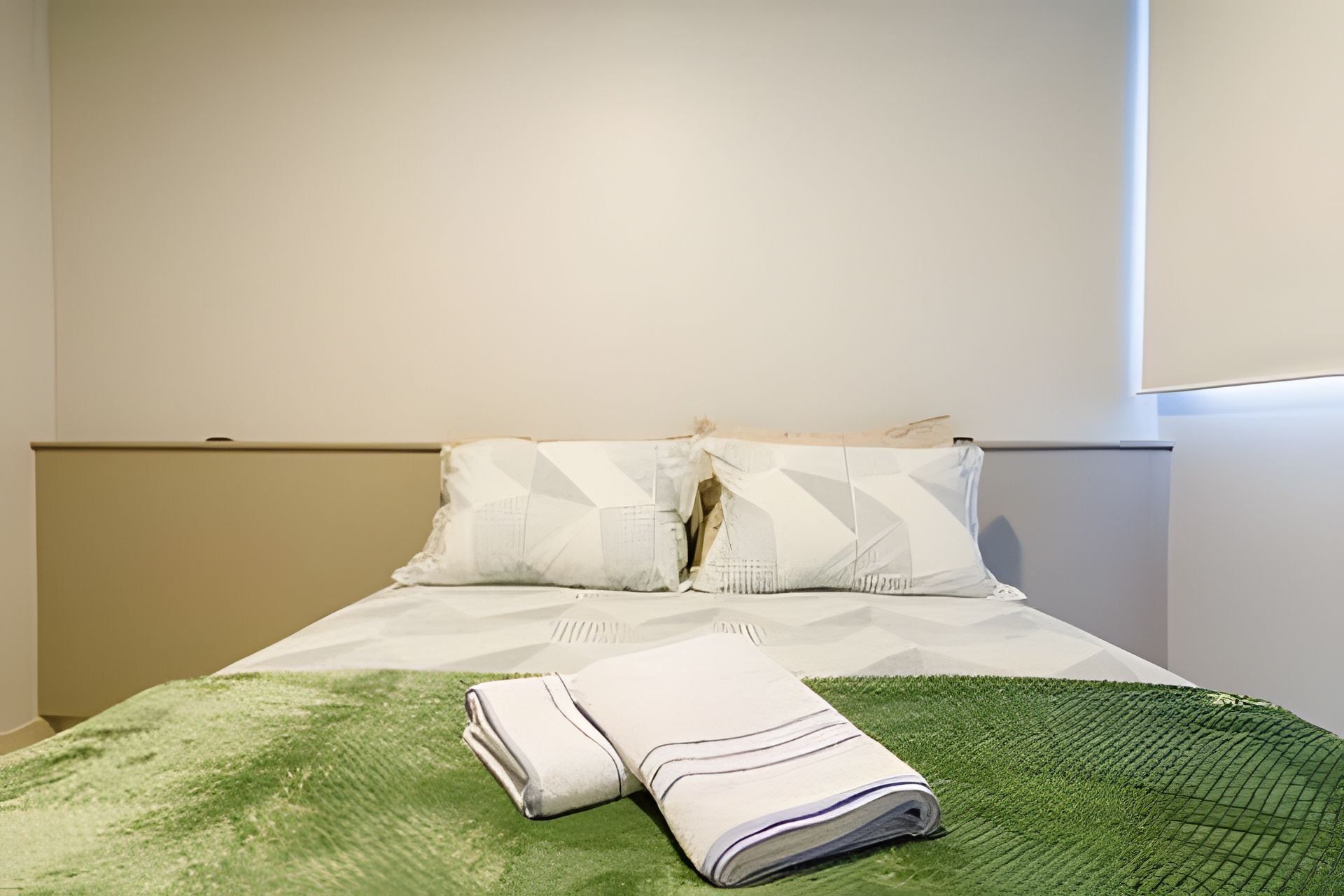 Cama com manta verde, duas almofadas e uma toalha dobrada.