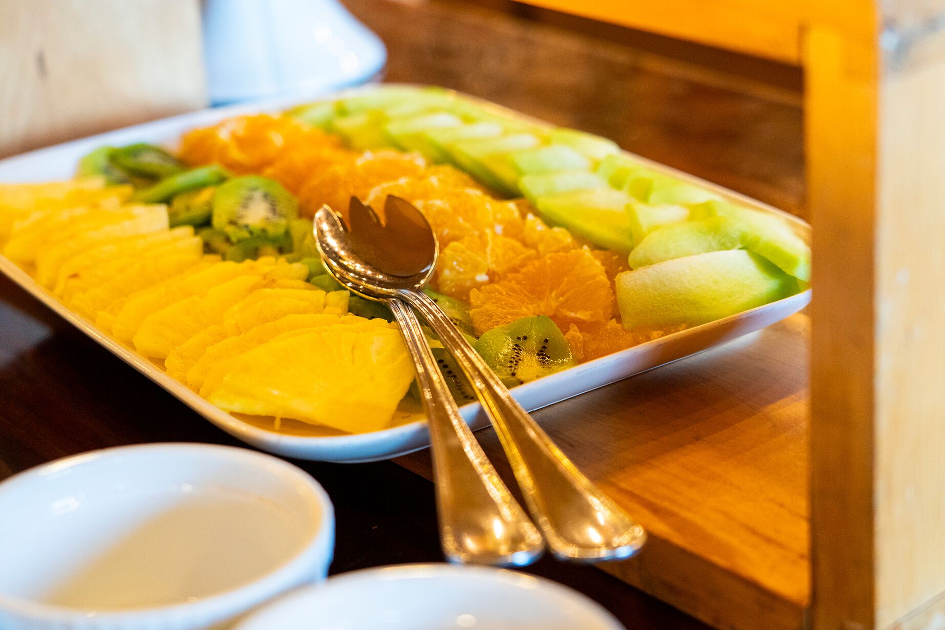 Um prato com frutas fatiadas, incluindo abacaxi, kiwi e melão, com uma colher ao lado.