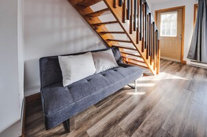 Uma sala de estar moderna com sofá cinza, escada de madeira e porta com janela.