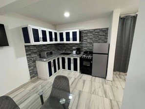 Uma cozinha compacta com armários brancos, fogão a gás, geladeira e micro-ondas.