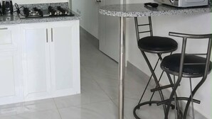 Cozinha com armários brancos, fogão a gás, micro-ondas e um banco de bar.