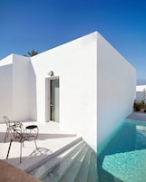 Um edifício moderno branco com piscina, uma porta e duas cadeiras.