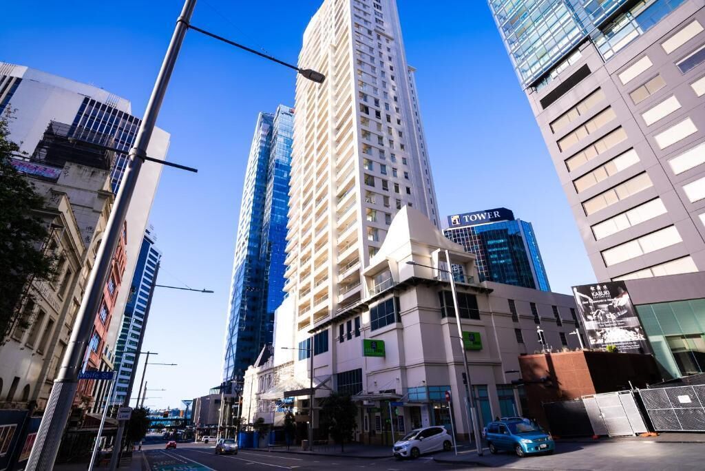 Paisagem urbana com edifícios altos e modernos, uma rua com carros e um céu azul límpido.