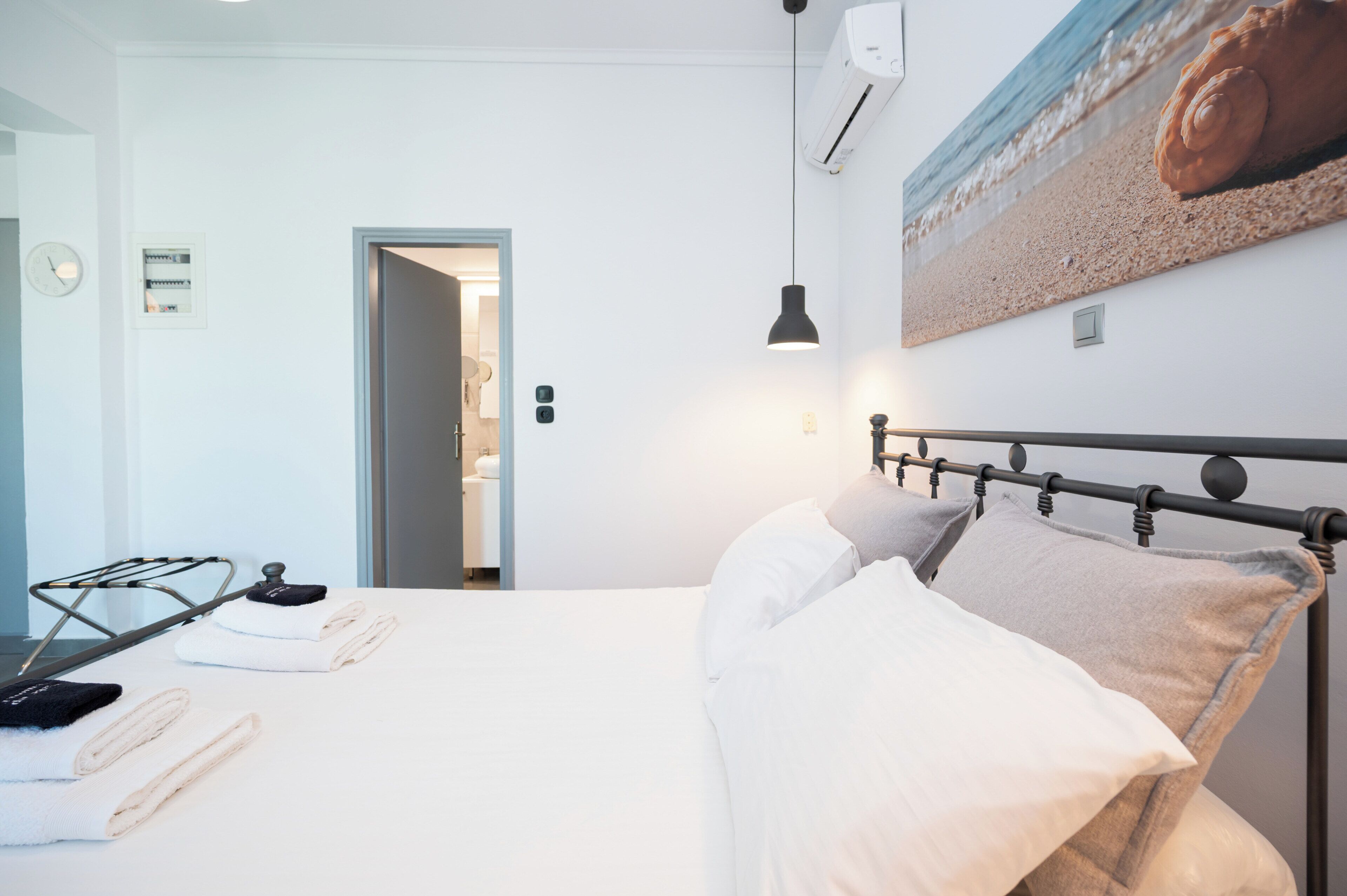 Uma cama bem arrumada com lençóis brancos, cabeceira de metal e ar condicionado fixado na parede.