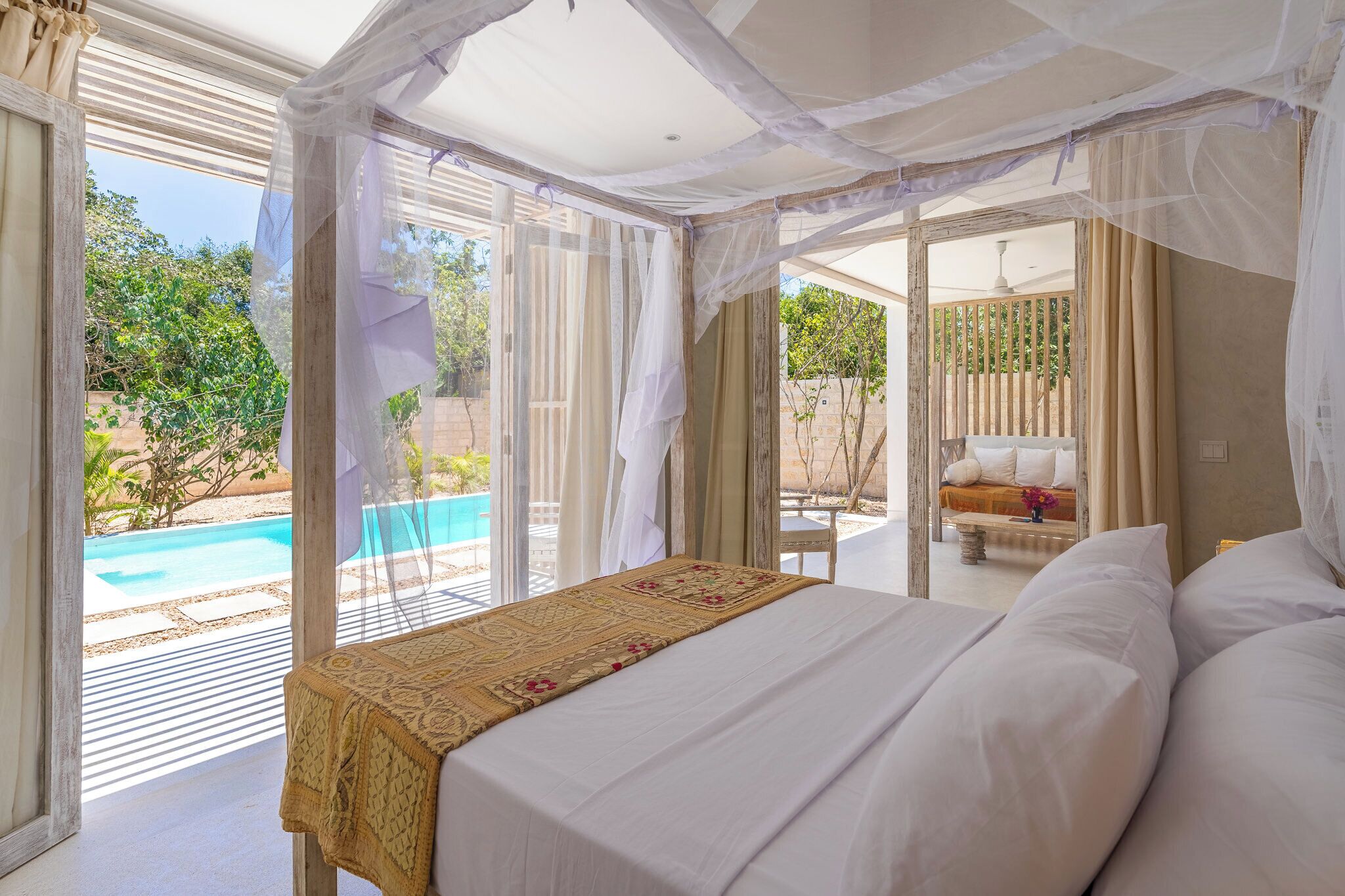 Quarto com cama, dossel e vista para uma piscina.