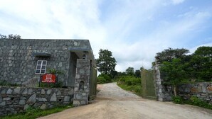 Um edifício de pedra com uma placa indicando um restaurante, uma estrada de terra que leva até ele e um portão.