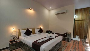 Quarto de hotel com uma cama grande, duas mesas de cabeceira, um criado-mudo, ar-condicionado fixado na parede e um guarda-roupa de madeira.