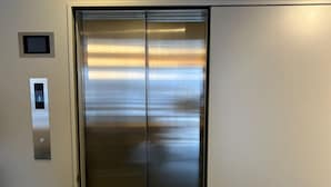 Porta de elevador metálica com painel de controle e uma pequena tela na parede.