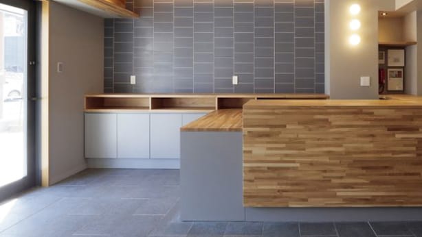 Cozinha moderna com bancada de madeira, painel de azulejos cinza e iluminação embutida no teto.