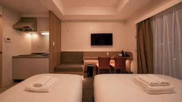 Quarto de hotel com duas camas, uma escrivaninha, uma cadeira, uma televisão e uma janela com cortinas.