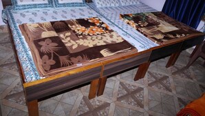 Uma cama com roupa de cama estampada com motivos florais e geométricos, uma cabeceira de madeira e um chão de azulejos.