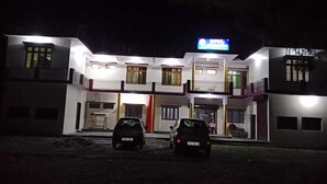Um edifício de dois andares com uma placa indicando que é um hotel. Há dois carros estacionados na frente.