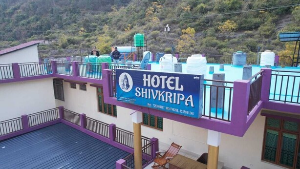Um hotel chamado Shivkripa com terraço no telhado, reservatórios de água e vista para uma paisagem montanhosa.