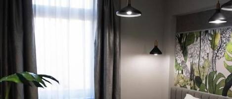 Um quarto moderno com cama, mesa de cabeceira e uma janela grande com cortinas.