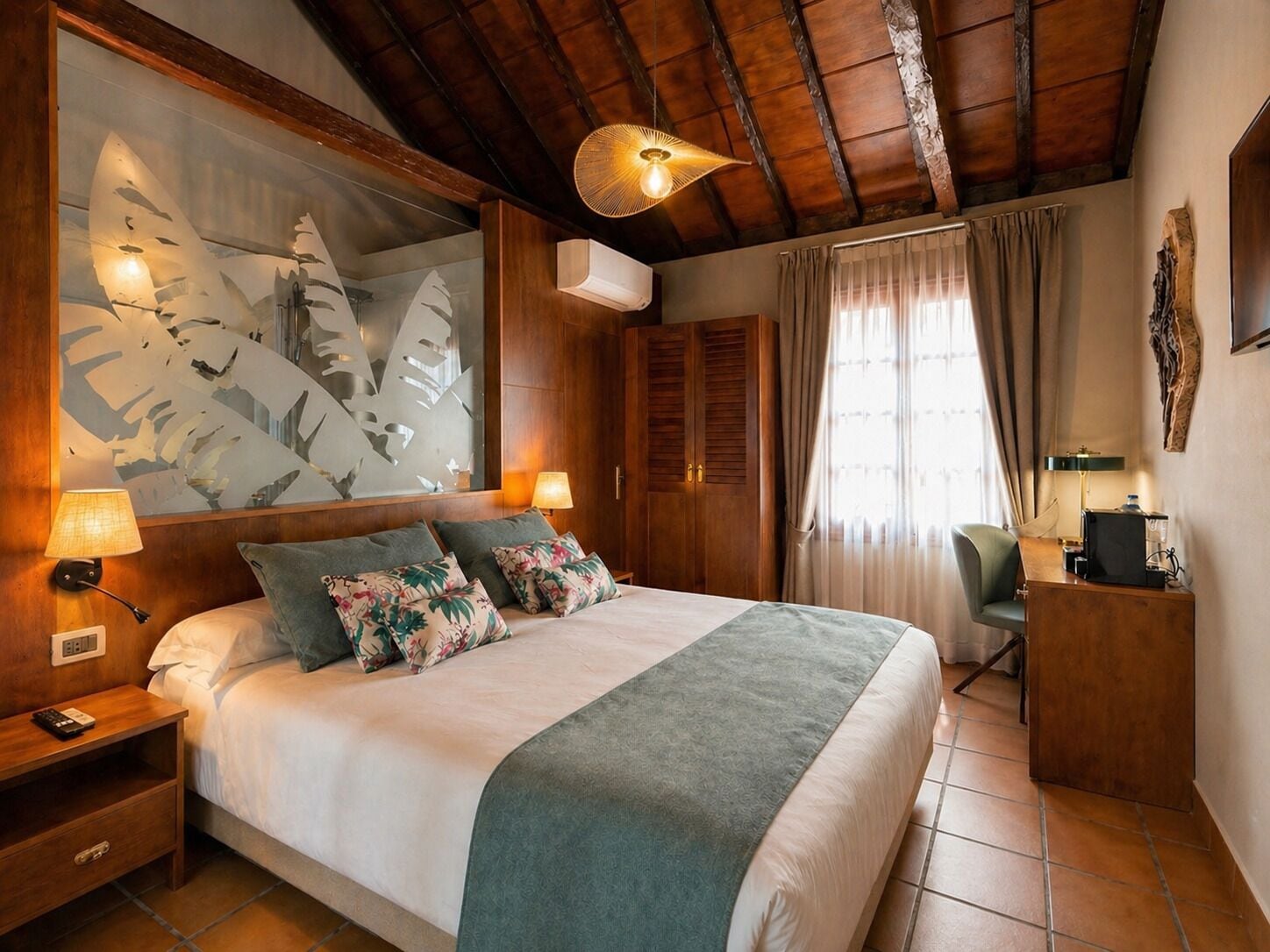 Quarto com cama, mesas de cabeceira, escrivaninha, cadeira, janela grande com cortinas e ventilador de teto.
