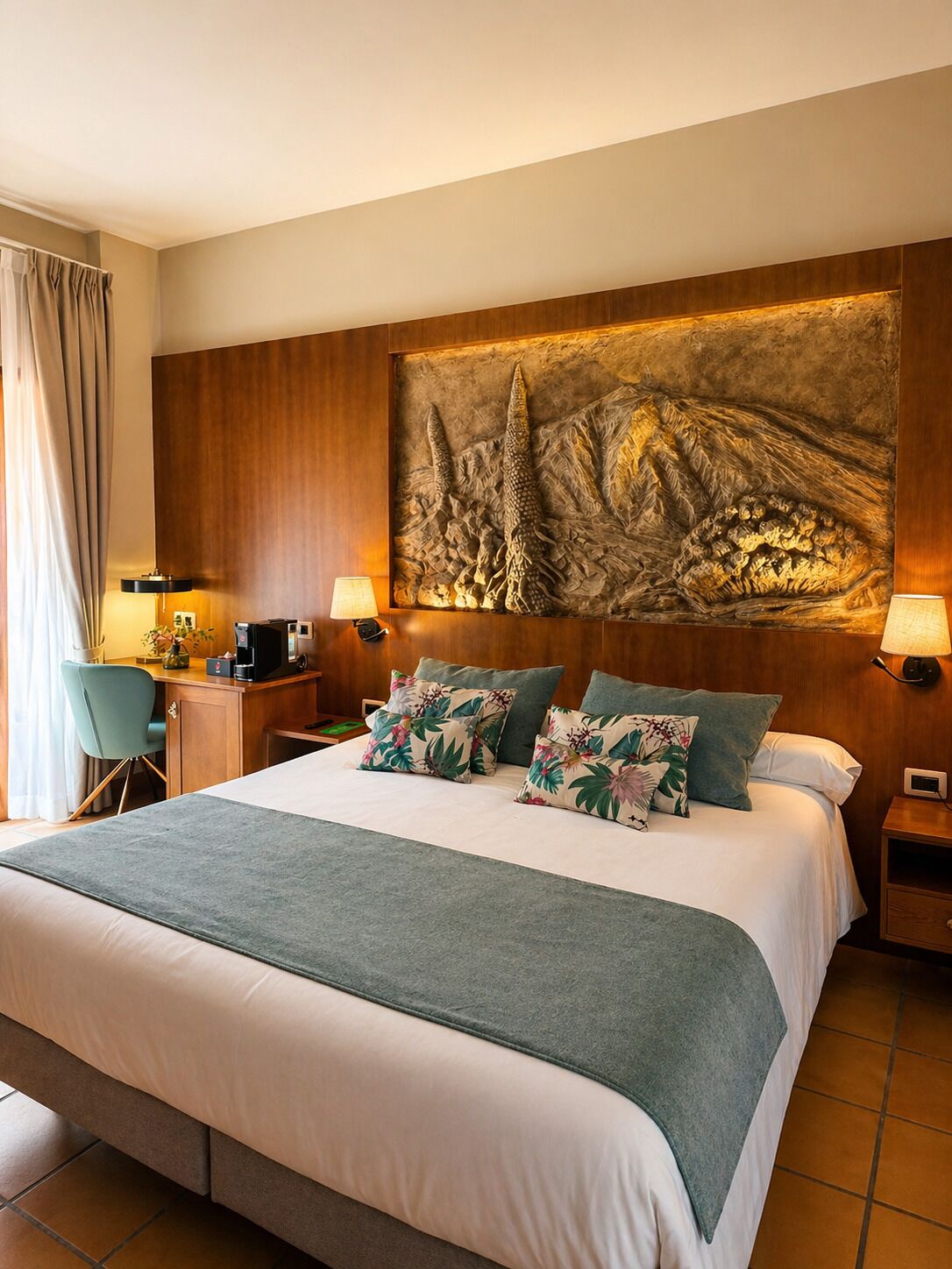Quarto de hotel com uma cama grande, duas mesas de cabeceira, uma escrivaninha com cadeira, um mural grande na parede e vista para o exterior.
