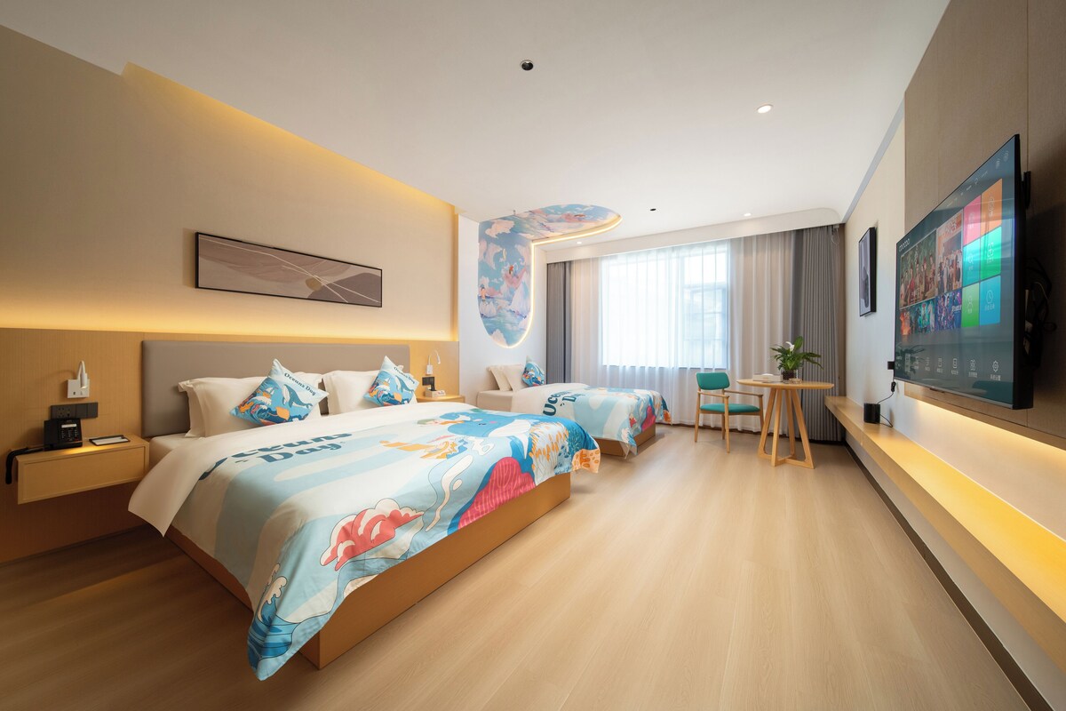 Quarto de hotel com uma cama grande, uma escrivaninha, uma cadeira, uma televisão e uma janela com cortinas.