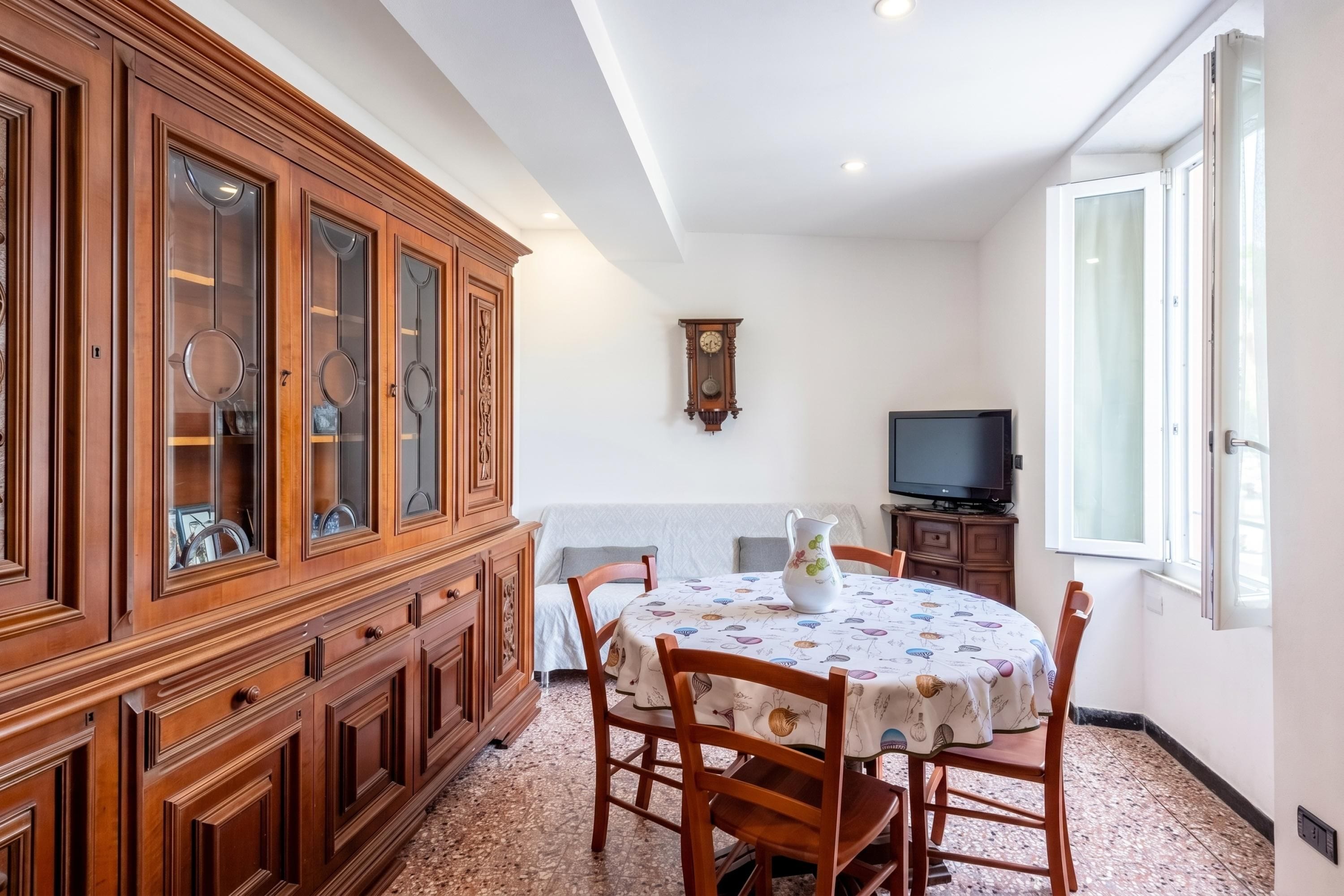 Uma sala de jantar com uma mesa, cadeiras, um armário, uma televisão e uma janela.