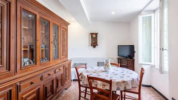 Uma sala de jantar com uma mesa, cadeiras, um armário, uma televisão e uma janela.
