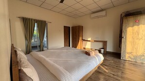 Quarto com cama, cortinas, ventoinha no teto, escrivaninha de madeira e ar condicionado.