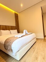 Quarto de hotel moderno com uma cama grande, cabeceira de madeira e iluminação ambiente acolhedora.