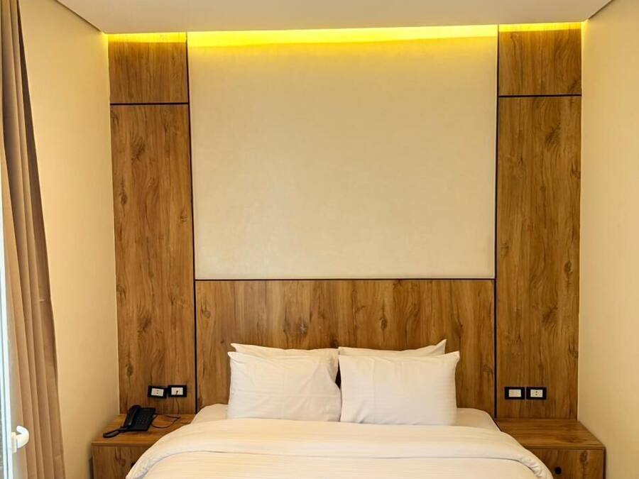 Quarto de hotel com uma cama grande, cabeceira de madeira, mesas de cabeceira e um telefone.