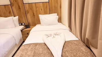 Quarto de hotel com duas camas, painel de cabeceira em madeira, manta marrom e travesseiro branco.