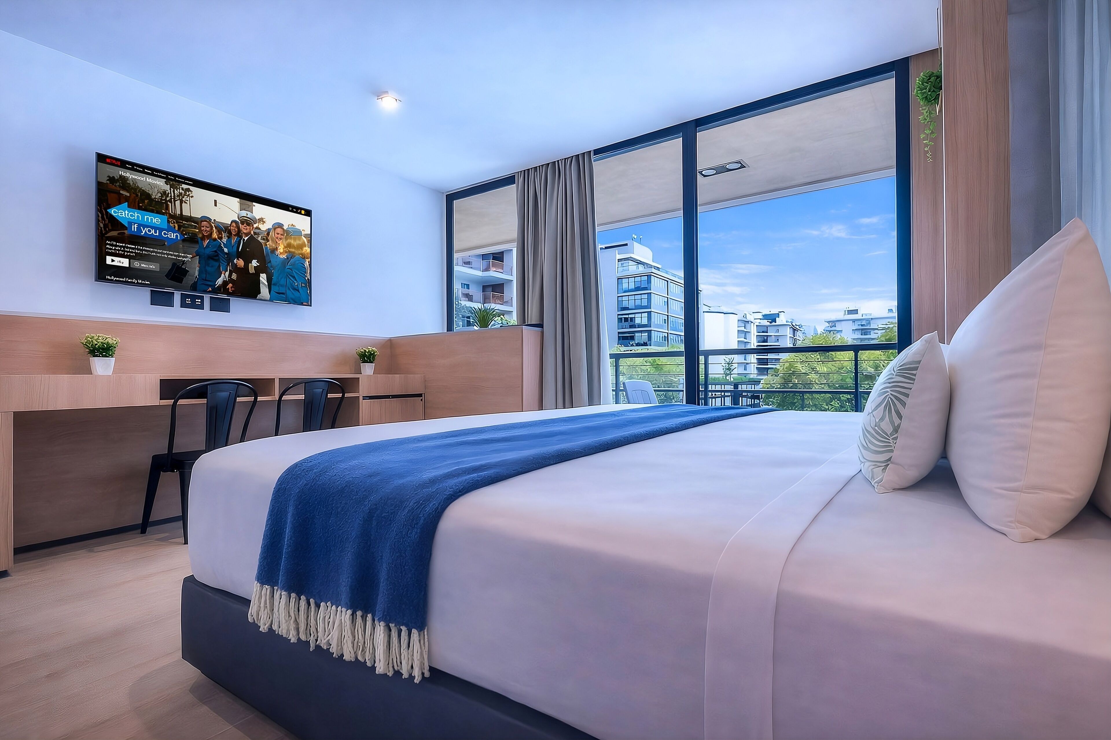 Quarto de hotel moderno com uma cama grande, uma escrivaninha e uma televisão na parede.