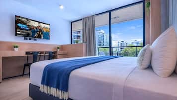 Quarto de hotel moderno com uma cama grande, uma escrivaninha e uma televisão na parede.