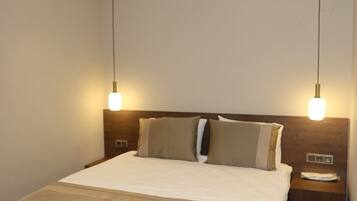 Quarto de hotel com uma cama grande, duas mesas de cabeceira, uma cabeceira de madeira e luminárias pendentes.