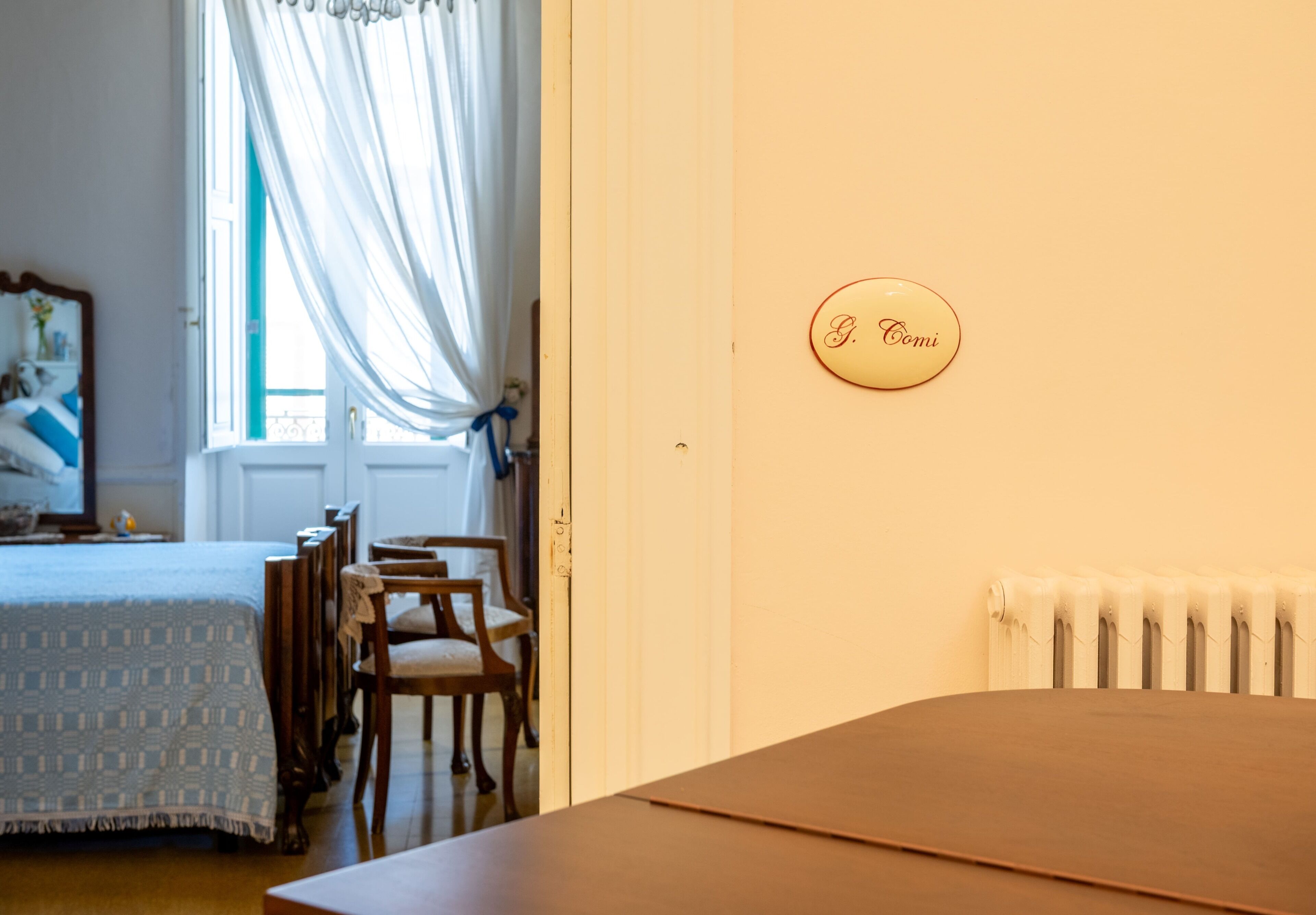 Quarto com cama, mesa, cadeiras, radiador e um aviso na parede.