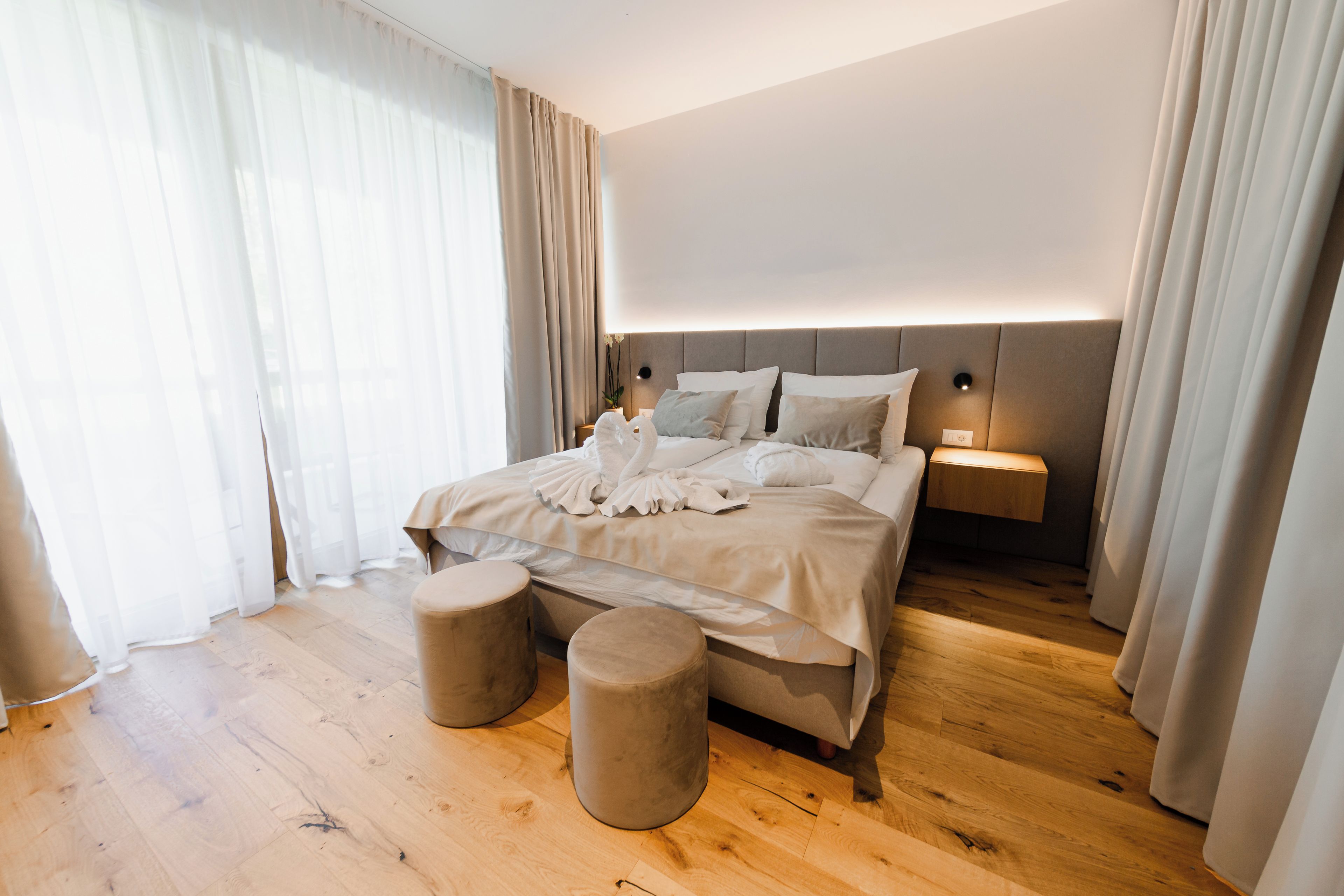Quarto moderno com cama grande, luminárias de cabeceira e piso de madeira.